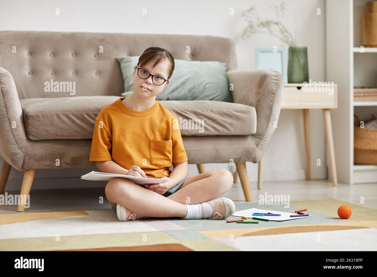 Full length portrait of teenage girl with Down syndrome sitting on ...