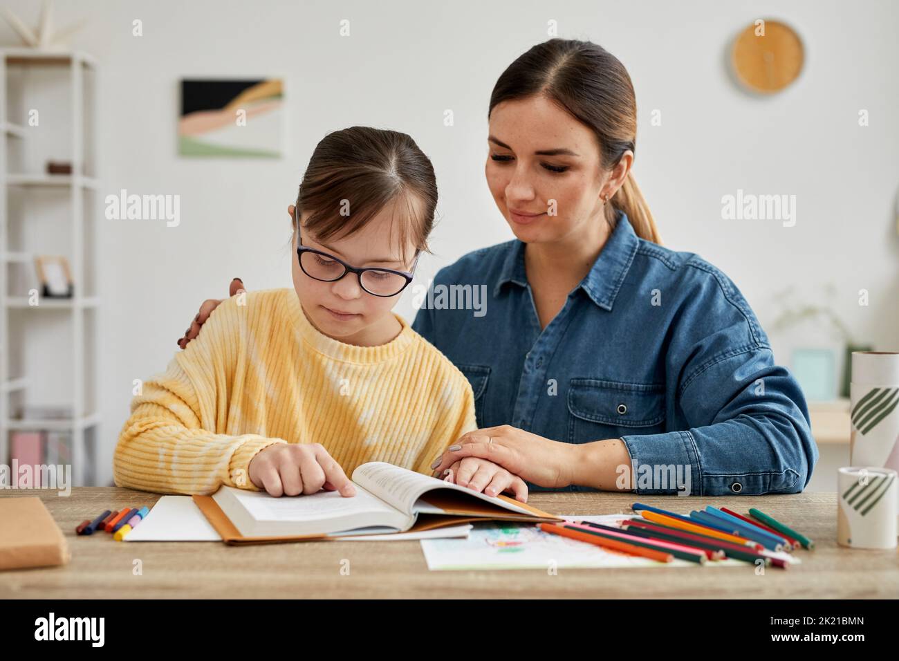 Portrait of mother and daughter with Down syndrome reading book ...