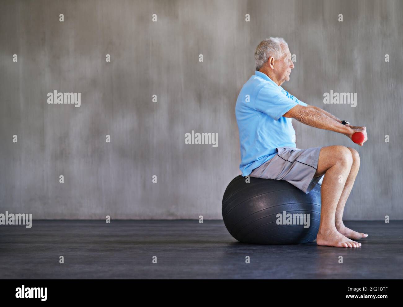 Combatting aging. an elderly man using weights while sitting on a swiss ...
