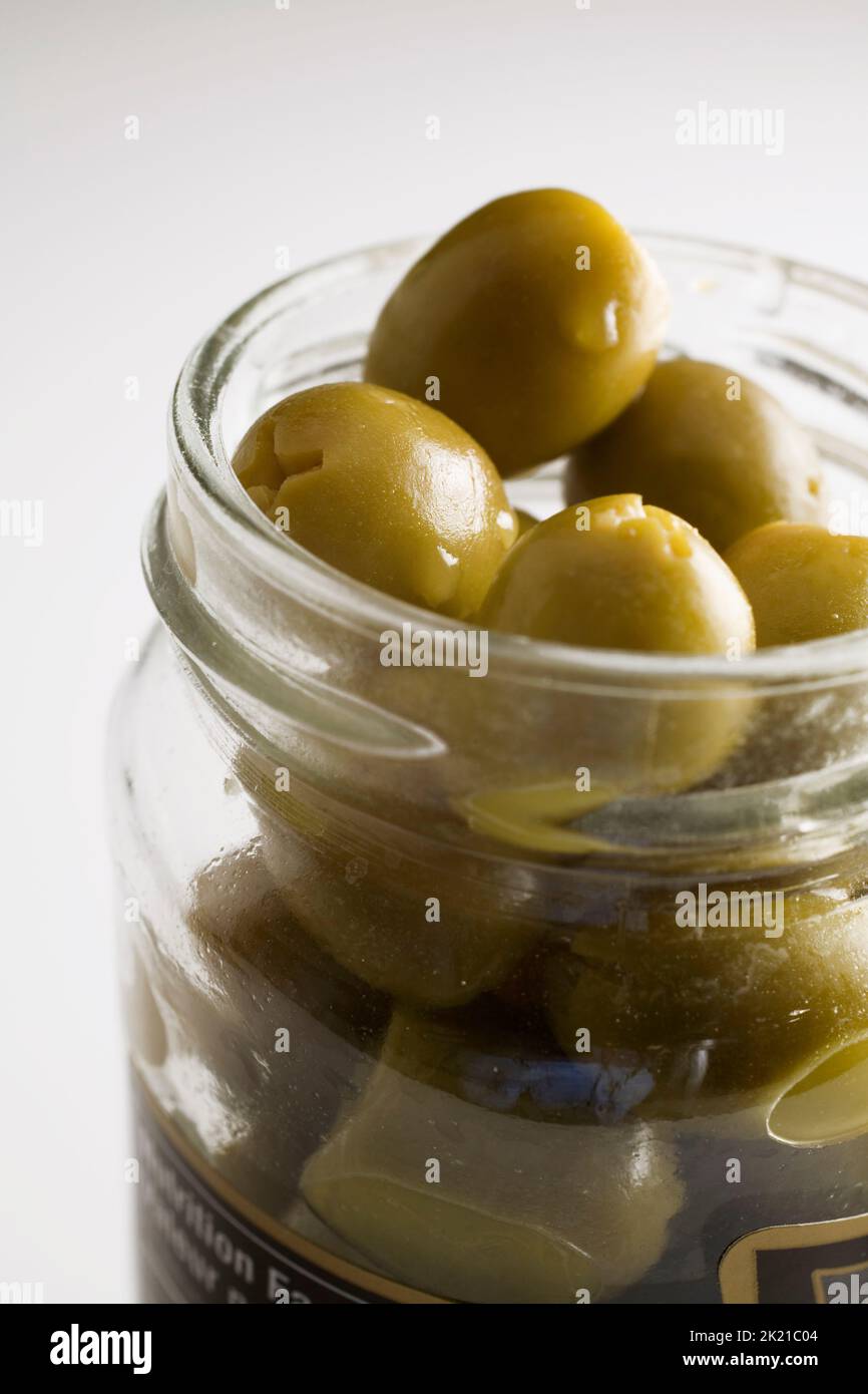 Close-up of green stuffed olives in glass packaging jar on light gray ...