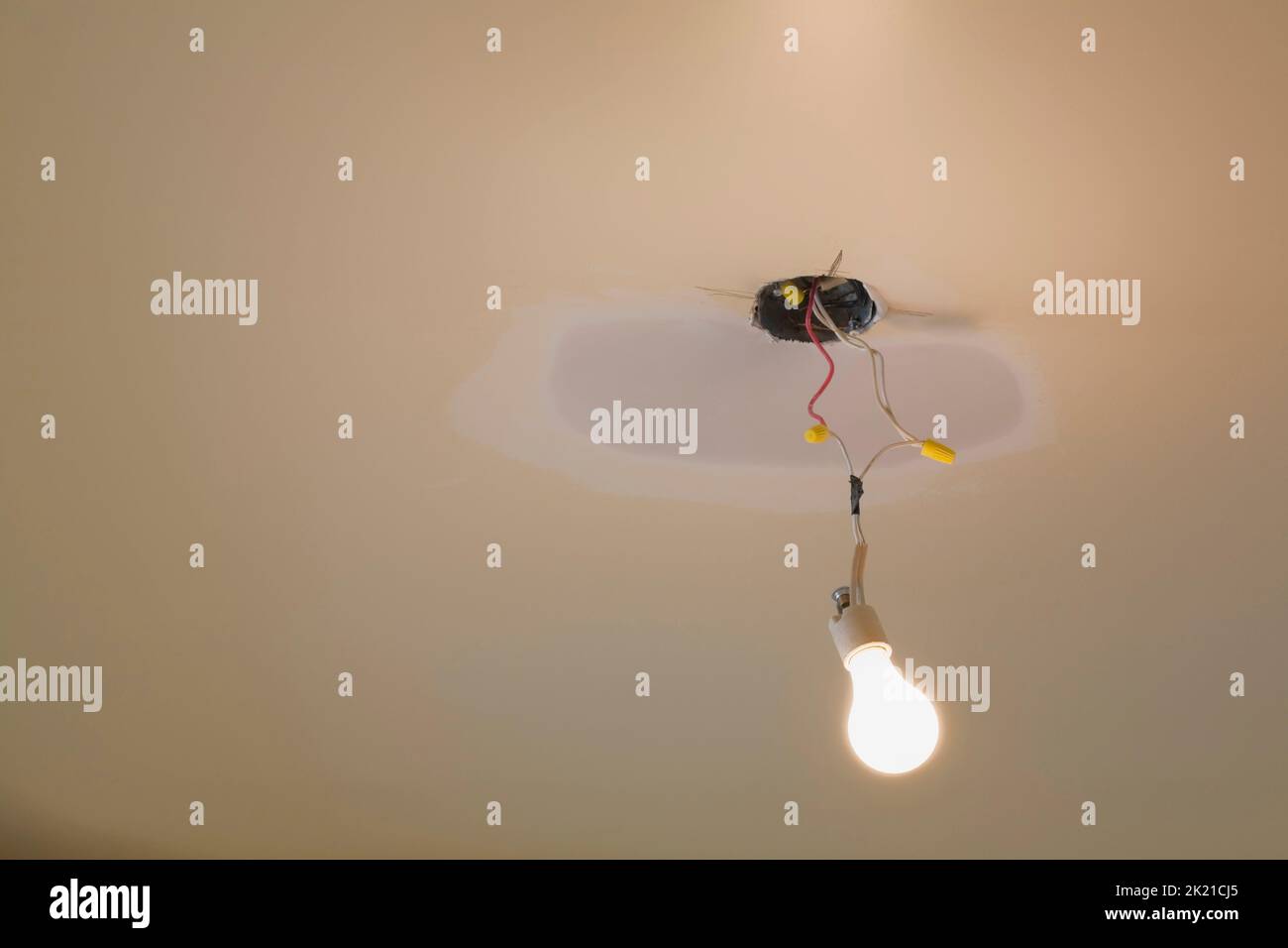 Incandescent lighttbulb dangling from ceiling plasterboard being ...