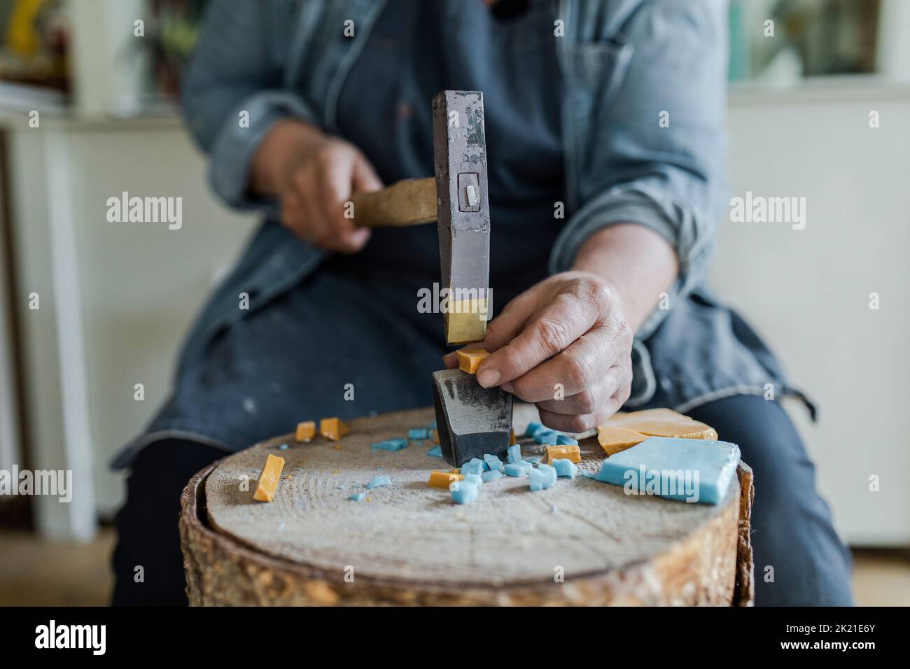 Female artist breaking mosaic glass with hammer and hardie in studio ...