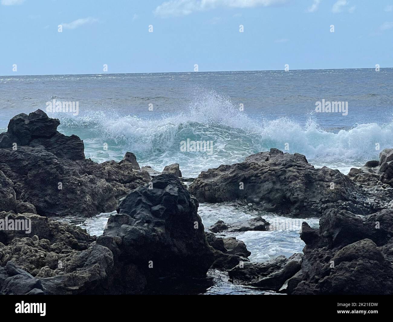 A mesmerizing view from a rocky beach of cloudy blue sky over the blue ...