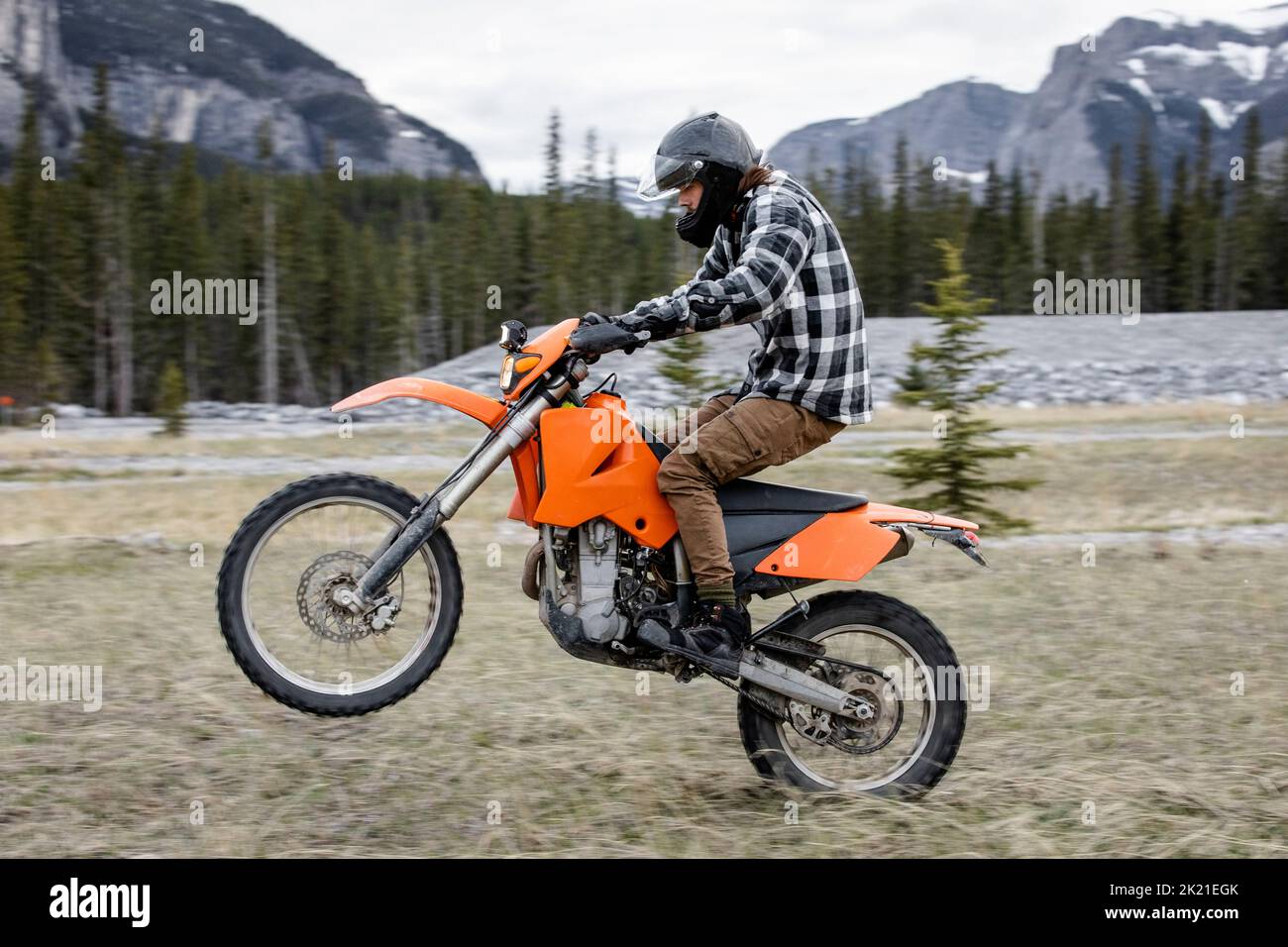 Man on dirt bike popping a wheelie in field below mountains, Canada ...
