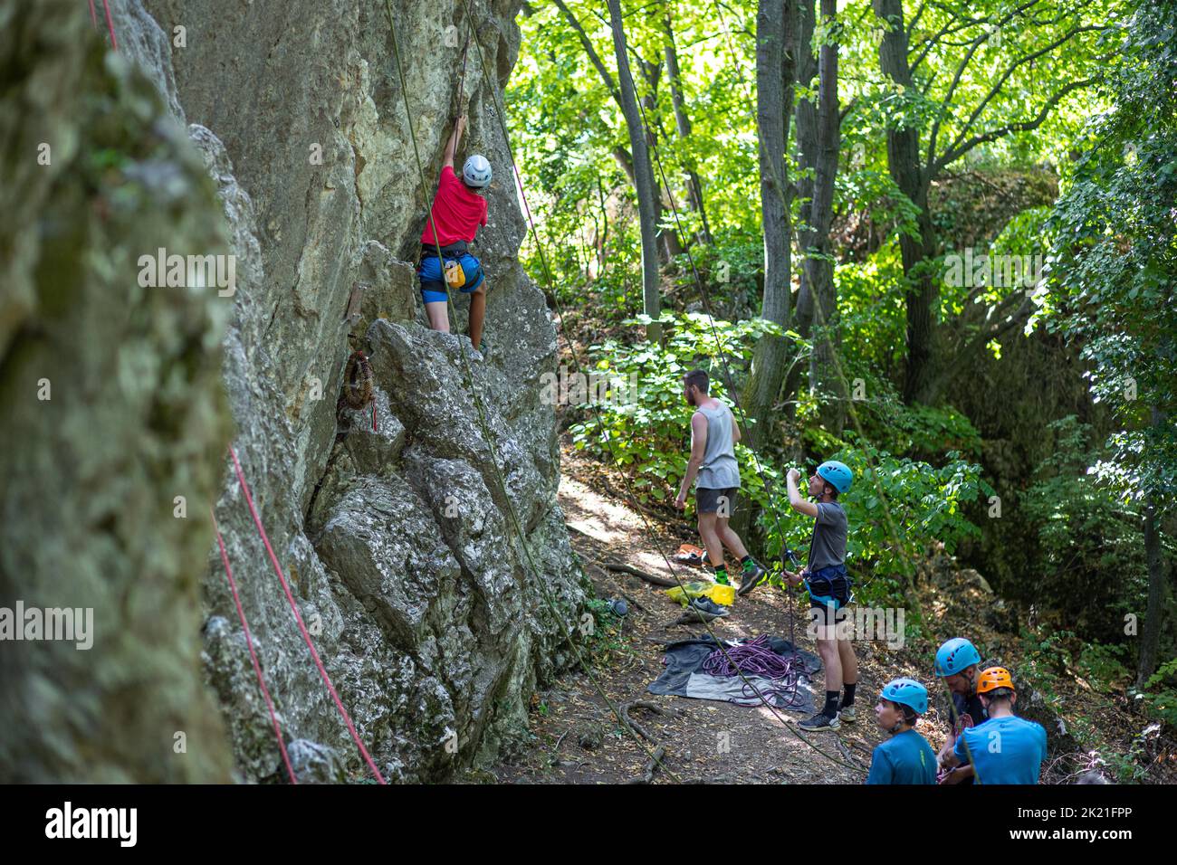 A group of rock climbers watching a youngster climb a cliff for the ...