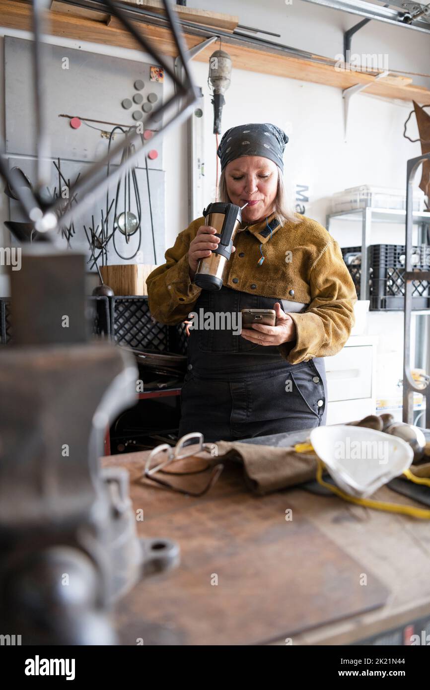 Female sculptor with smart phone taking coffee break in workshop Stock ...