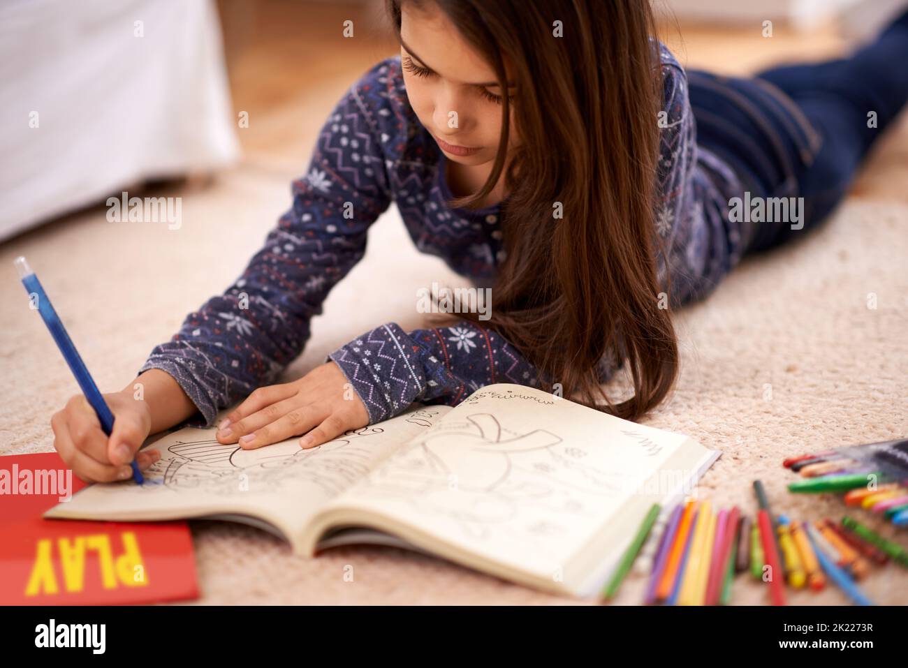 Every child is an artist. A young girl coloring while lying on the ...