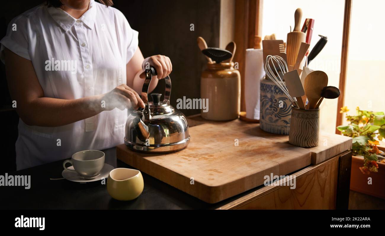 The comforts of home. a young woman making a cup of tea in her kitchen ...
