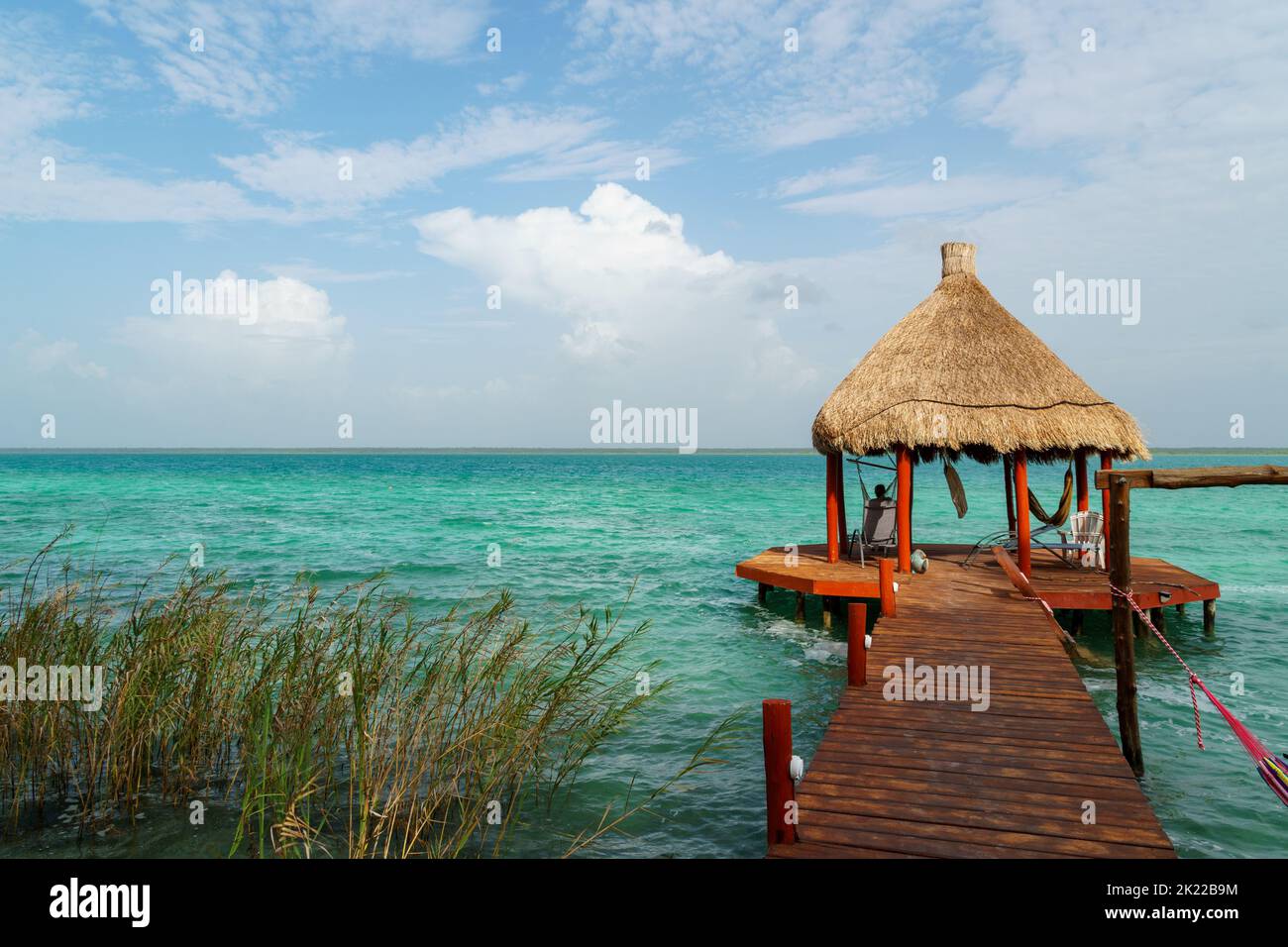 Thatched hut at the end of a pier jutting out into the blue water of ...
