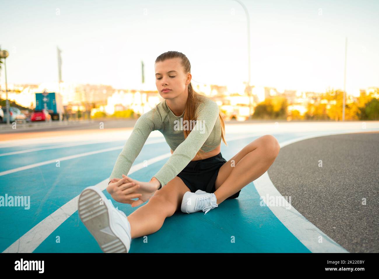 Sportswoman sitting and stretching on blue track field. Woman runner ...