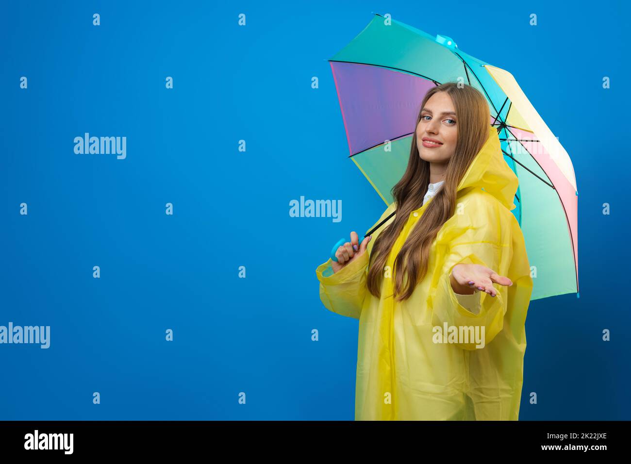 Young woman in yellow raincoat with rainbow umbrella against blue ...