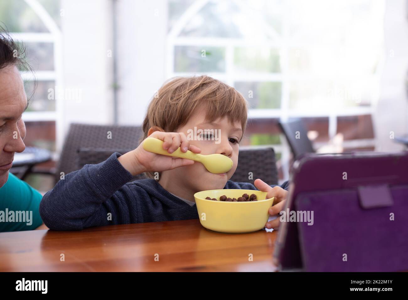 Little boy sit on chair at table and watch cartoon on tablet computer ...