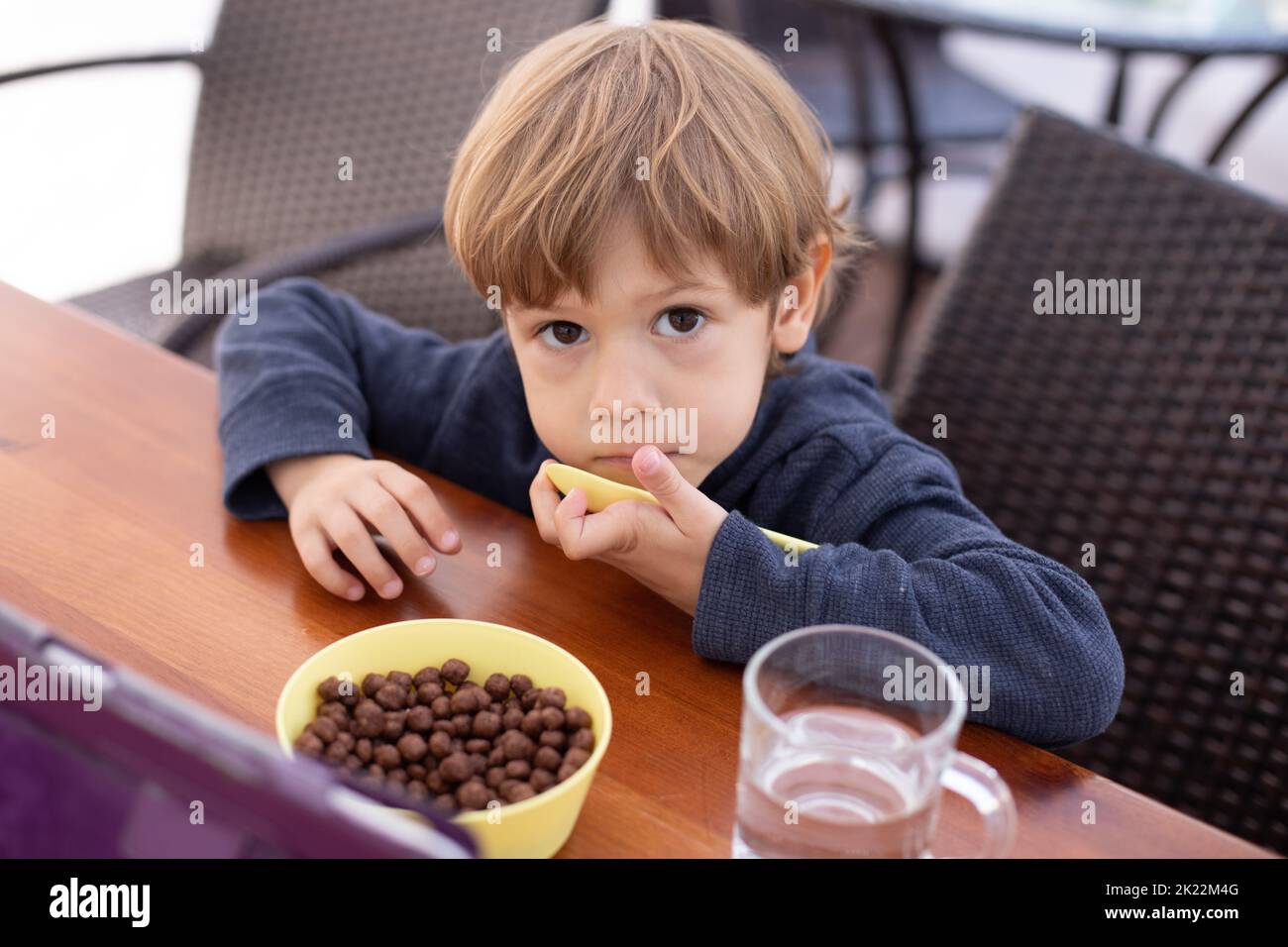 Unhappy little boy sit at table and watch cartoon on tablet computer ...
