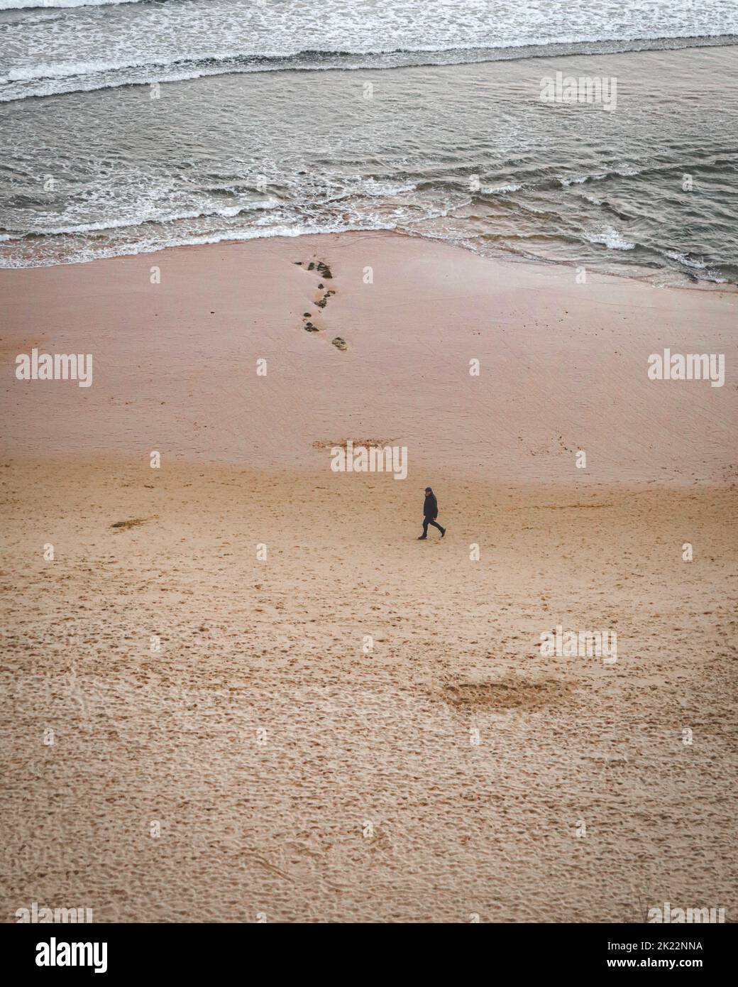 An aerial view of a person walking on sandy beach on a cold windy day ...