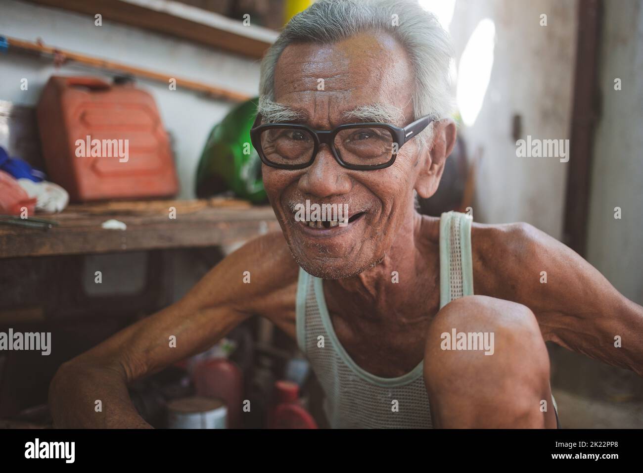 An old man with eye glasses smiling in a small local shop in Yogyakarta ...