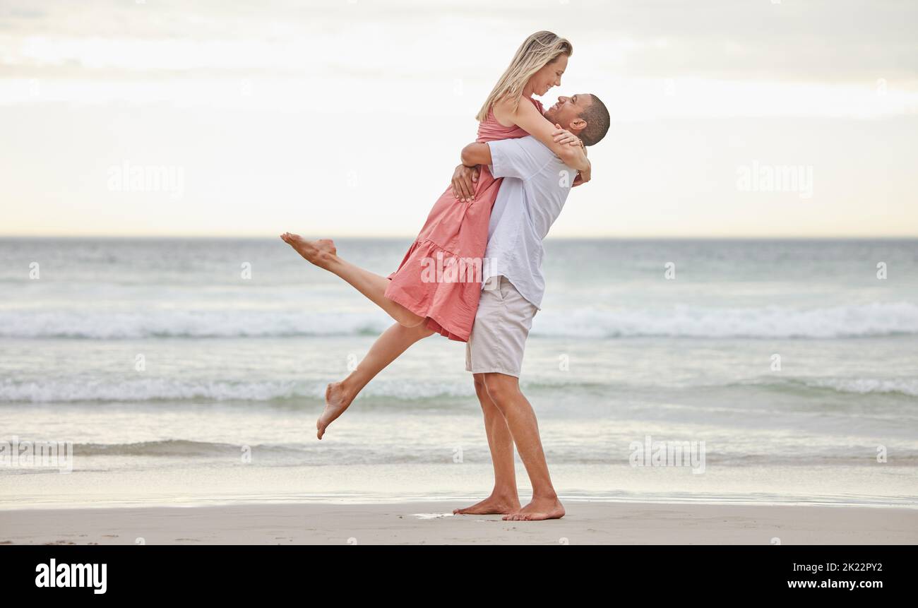 Interracial Couple Love And Hugging On A Beach By The Water In Holiday