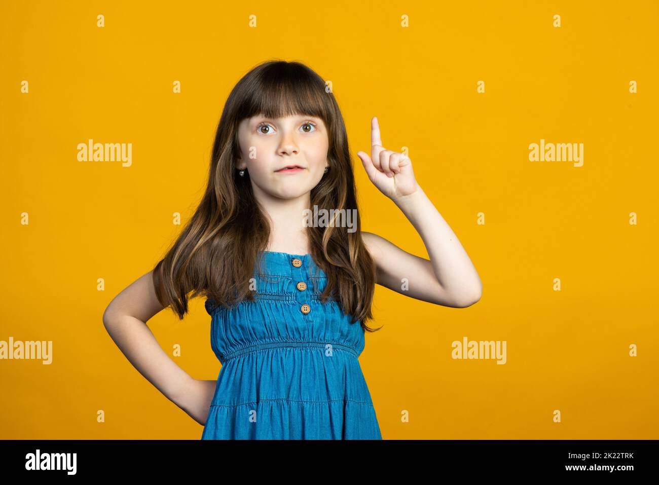 Cute little girl is surprised and raised her index finger up. An idea ...
