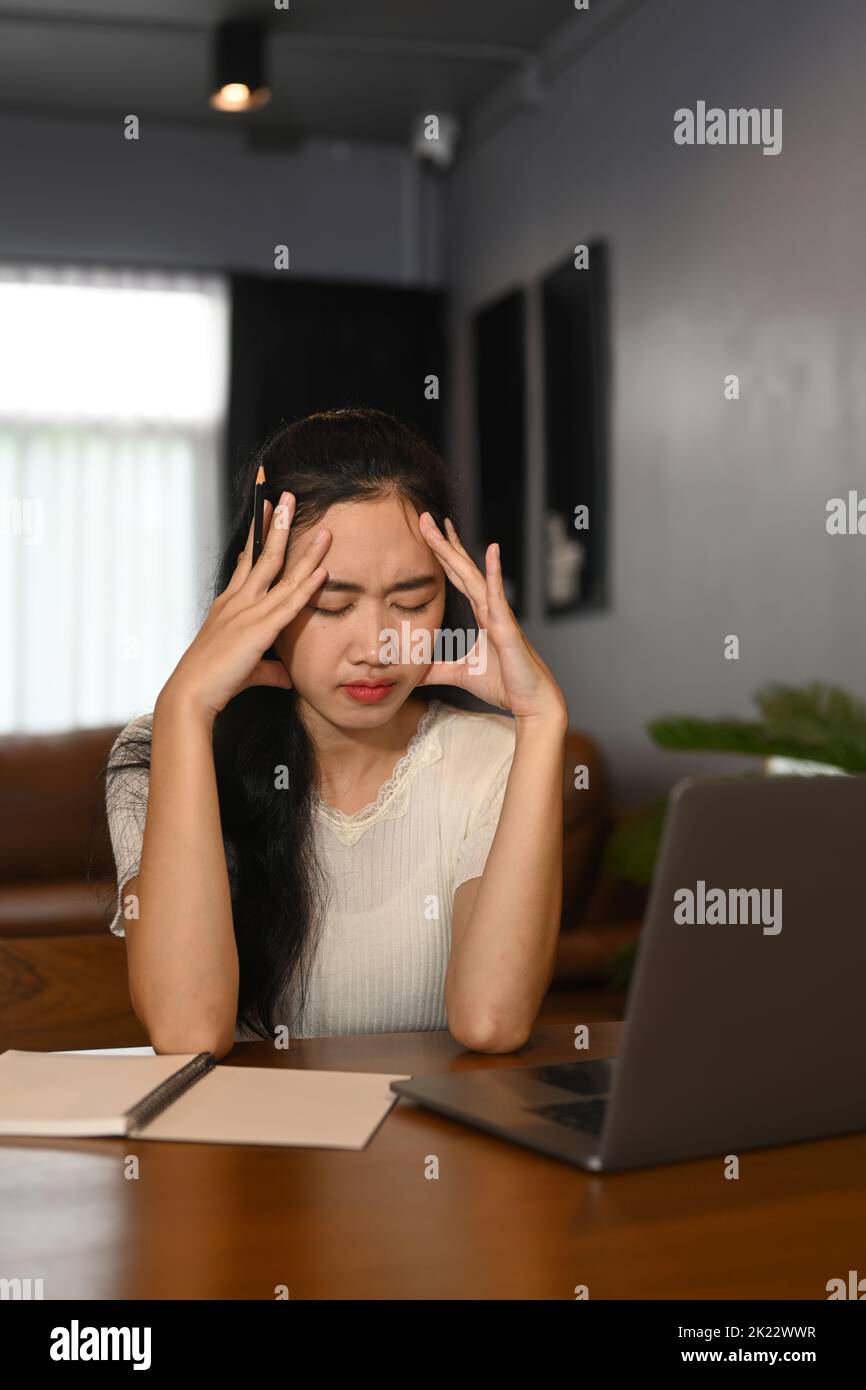 Tired asian female freelancer holding her head in hands, exhausted from ...