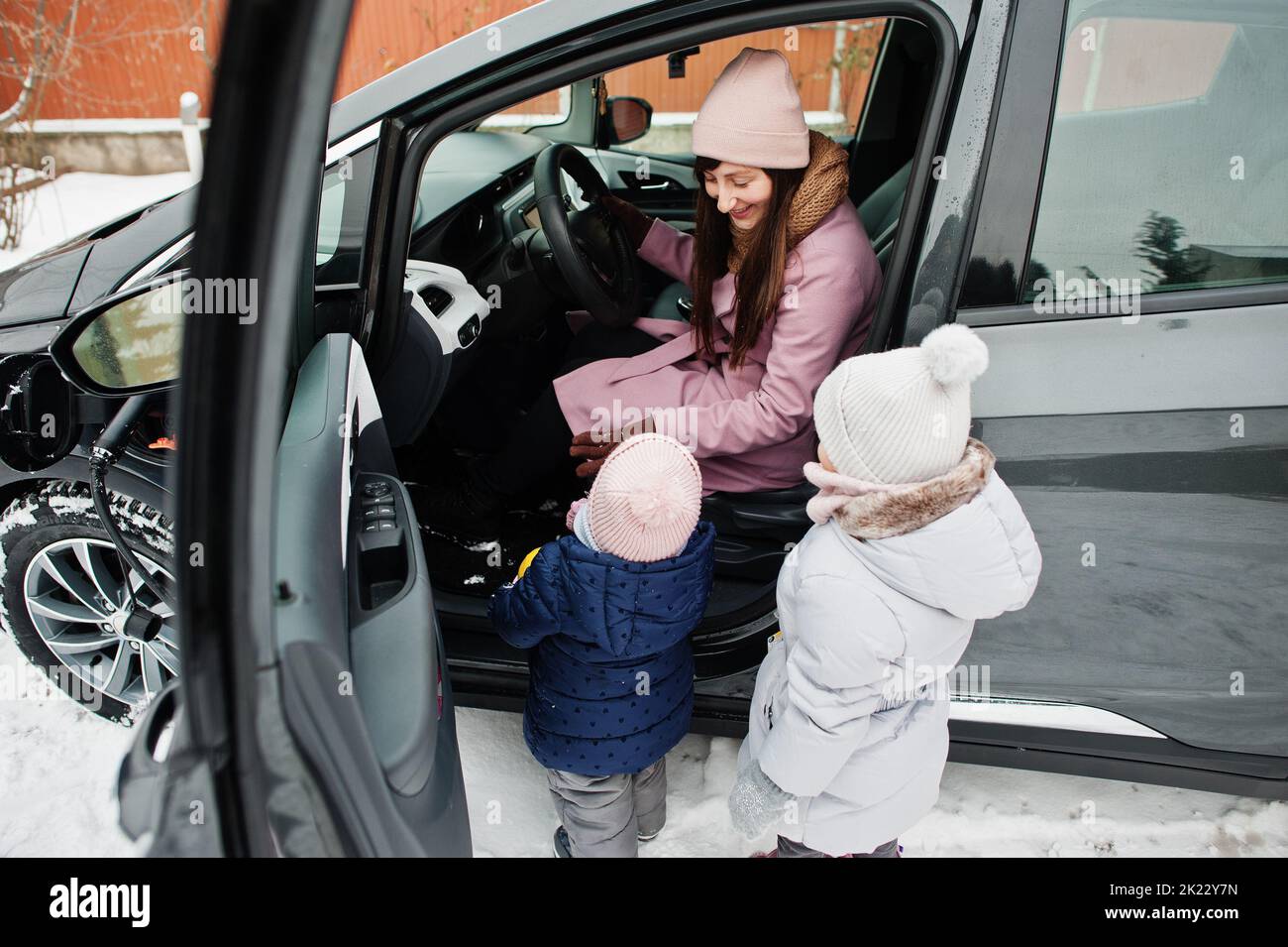 Young mother with kids charging electric car in the yard of her house ...