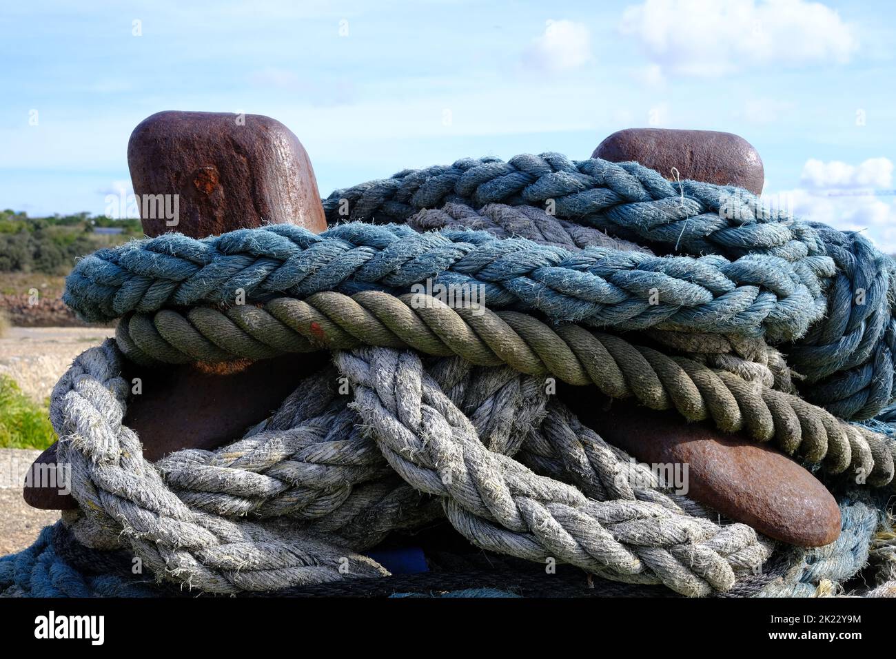 Ropes twisted and coiled round a rusty iron tethering on the harbour ...