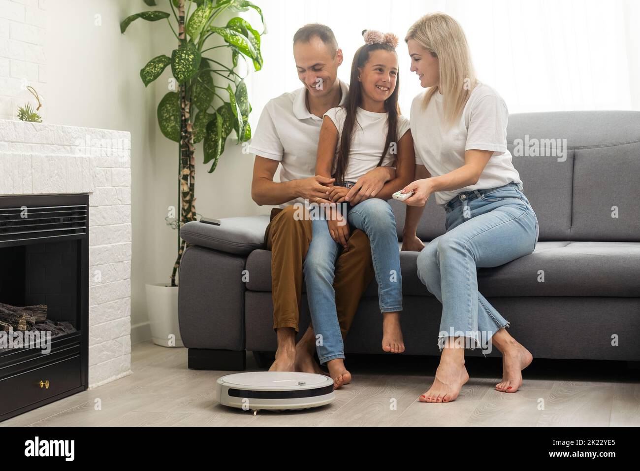 Young family resting on the couch while robotic vacuum cleaner doing ...