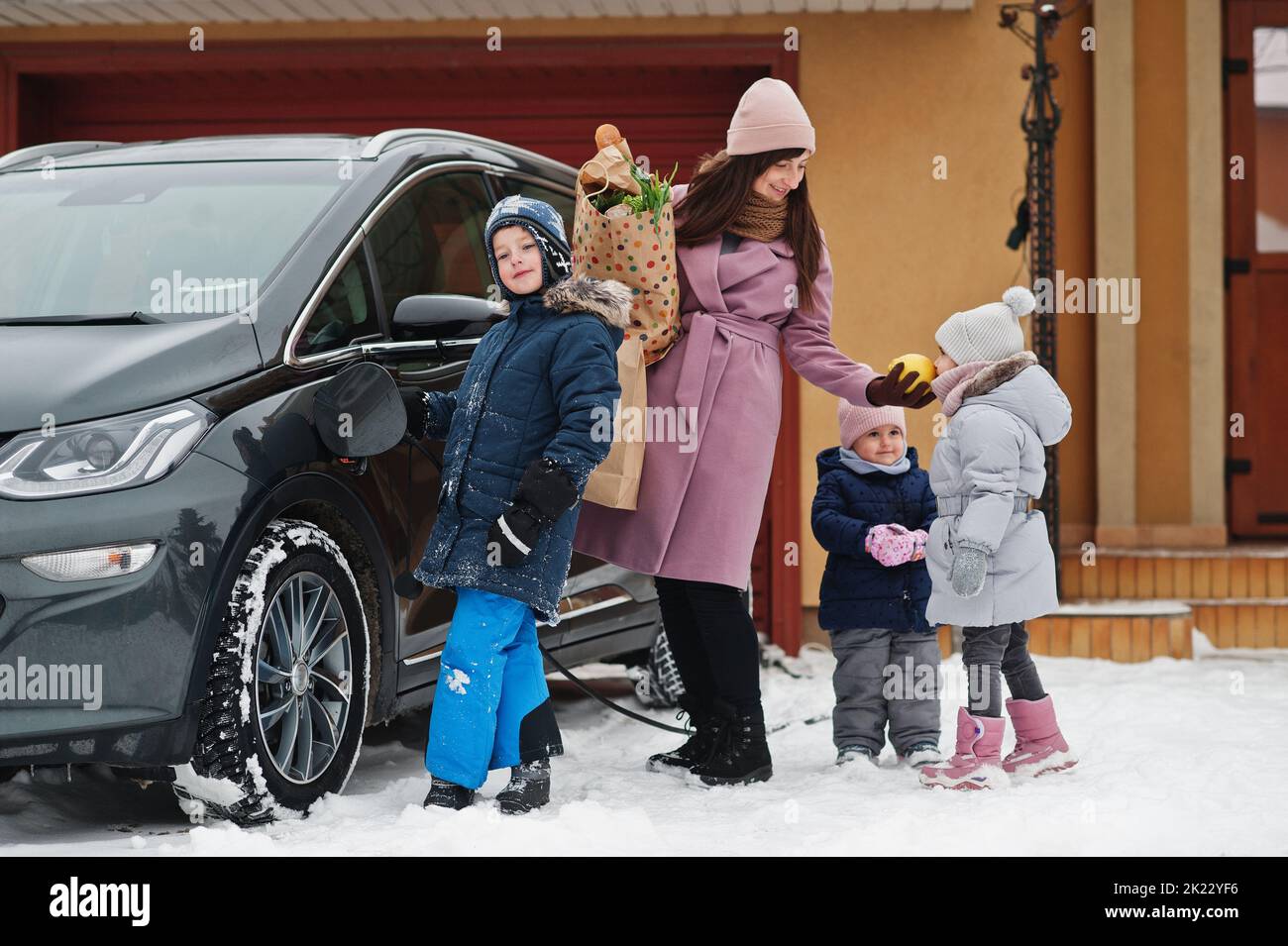 Young woman with kids hold eco bags and charging electric car in the ...