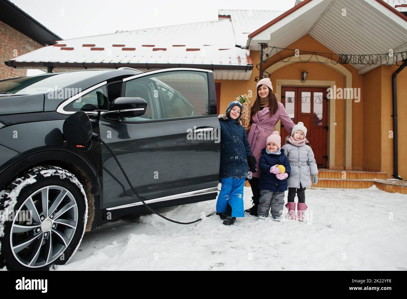 Young woman with kids hold eco bags and charging electric car in the ...
