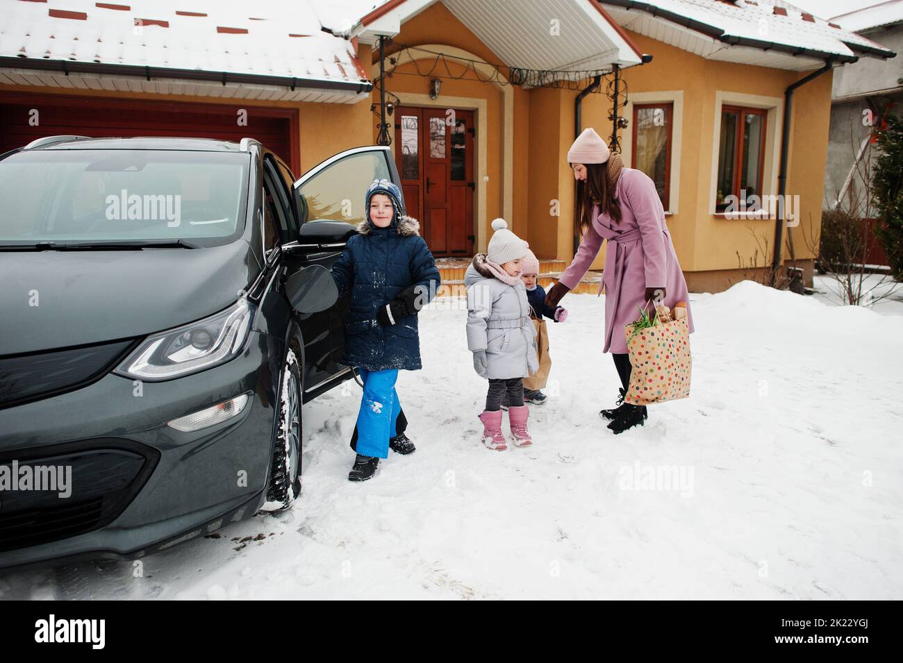 Young woman with kids hold eco bags and charging electric car in the ...