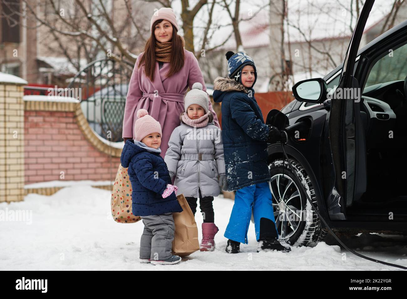 Young woman with children hold eco bags and charging electric car in ...