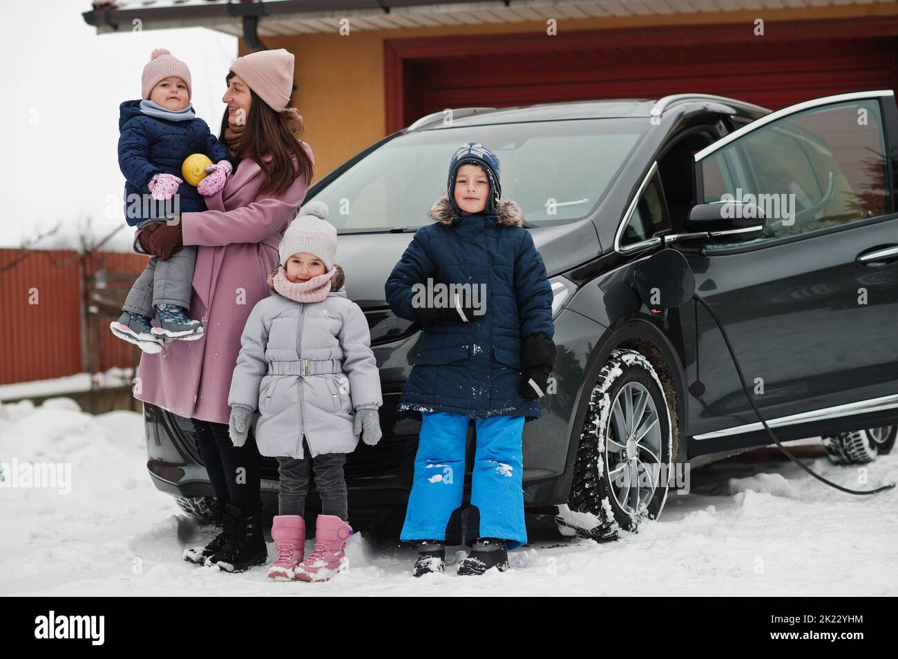 Young mother with kids charging electric car in the yard of her house ...