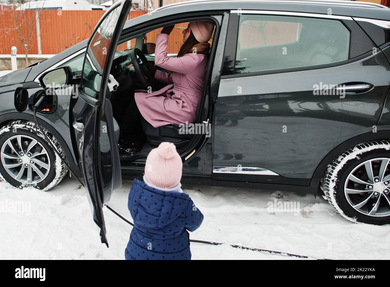 Young mother with baby girl charging electric car in the yard of her ...