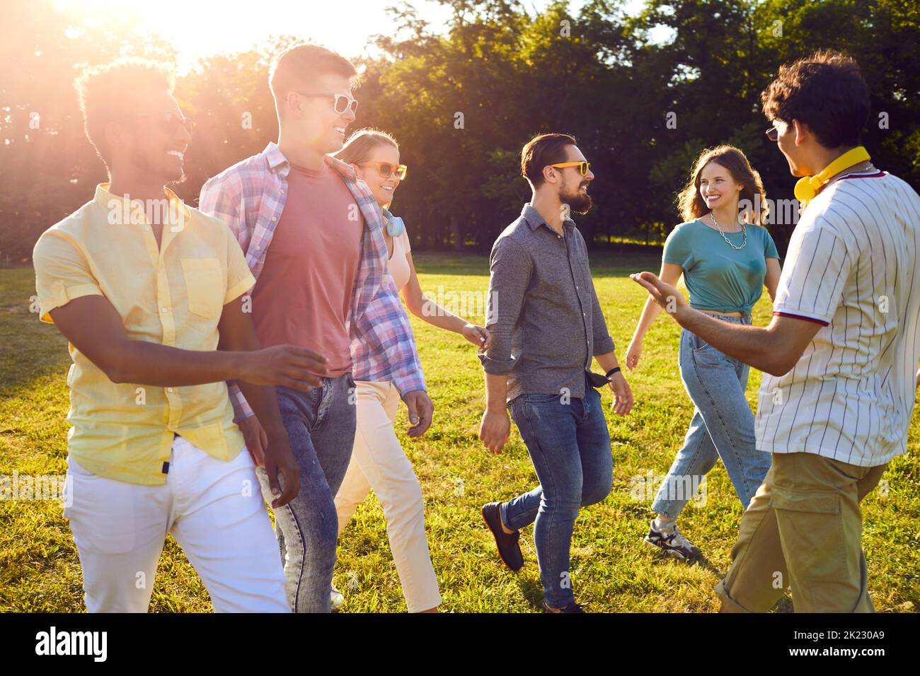 Group of happy young multiracial men and women walking in a green park ...