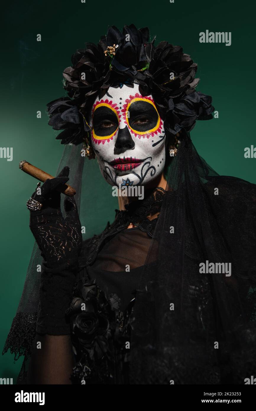 Woman in mexican day of death makeup and black costume holding cigar on ...