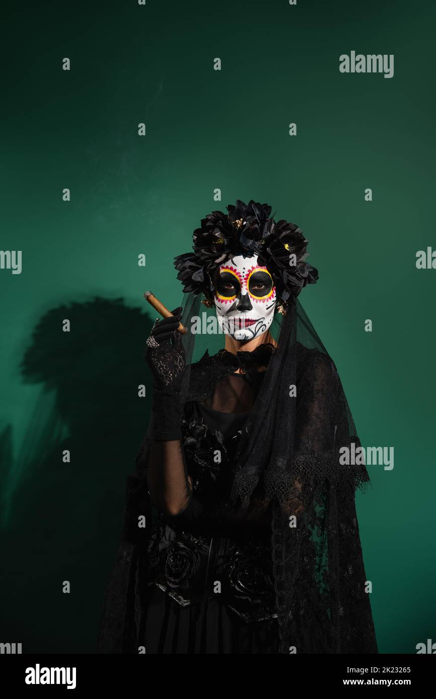 Woman in santa muerte halloween costume holding cigar on green ...