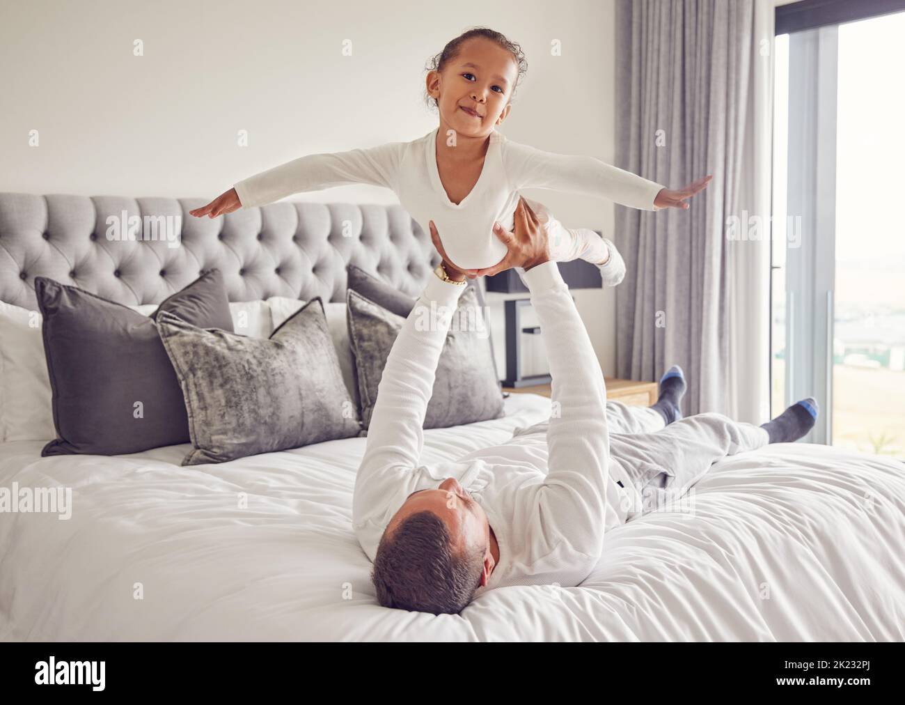 Father lifting child in air on bed, playing and bonding in bedroom of ...