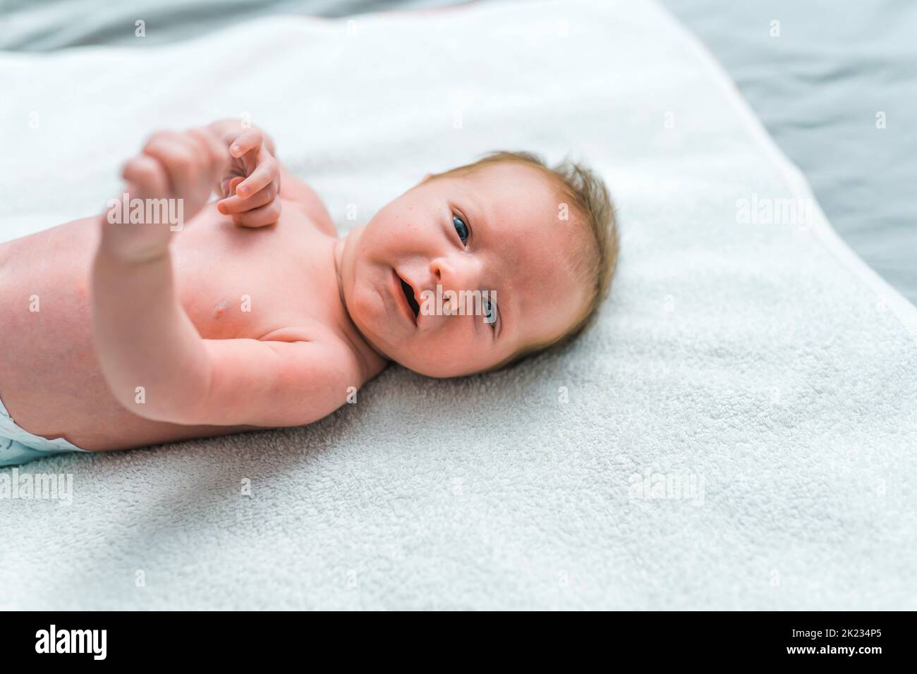 White newborn baby in a diaper lying on blanket on floor looking into ...