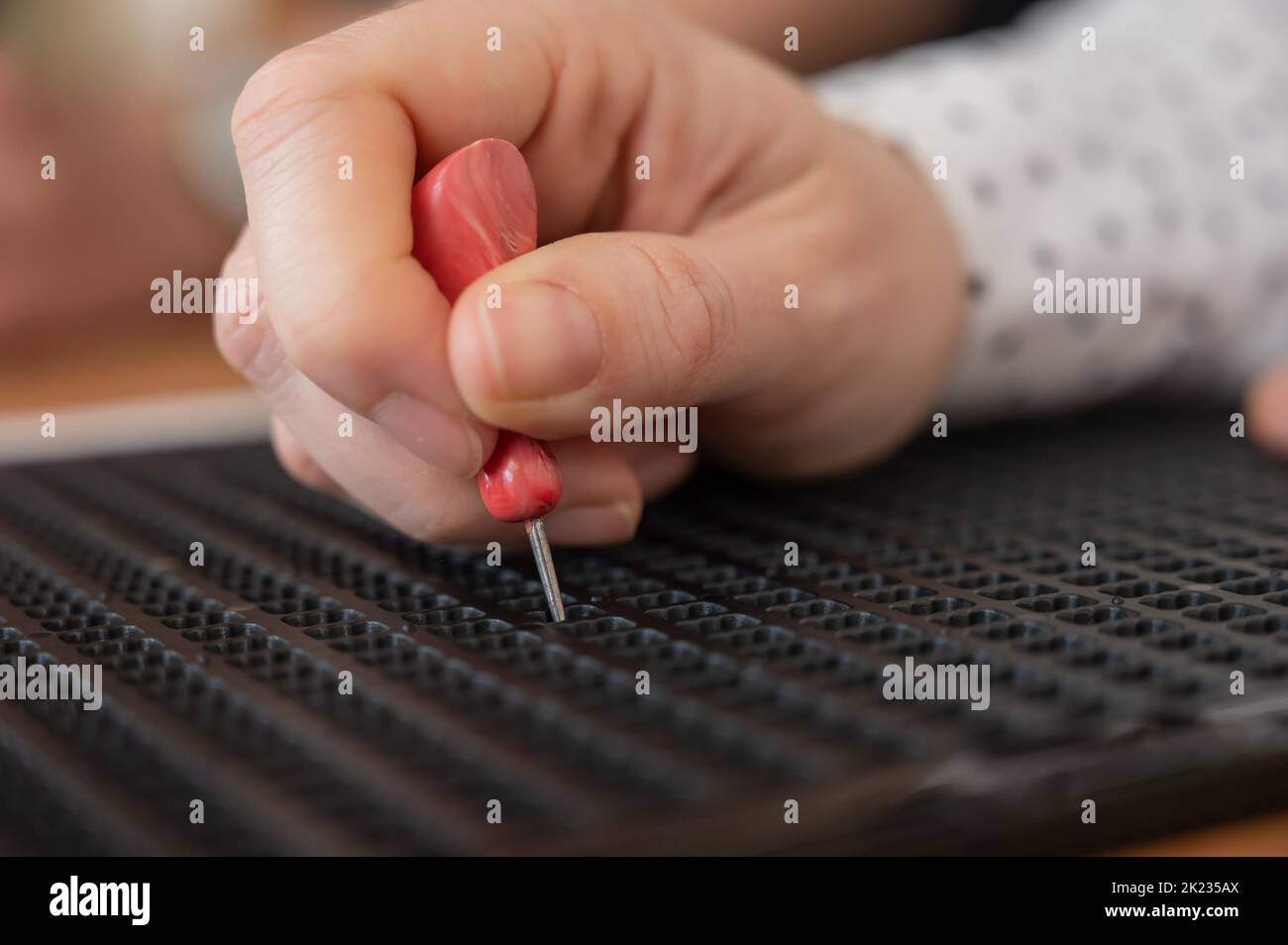A woman uses a special stencil and stylus to write a letter in braille ...