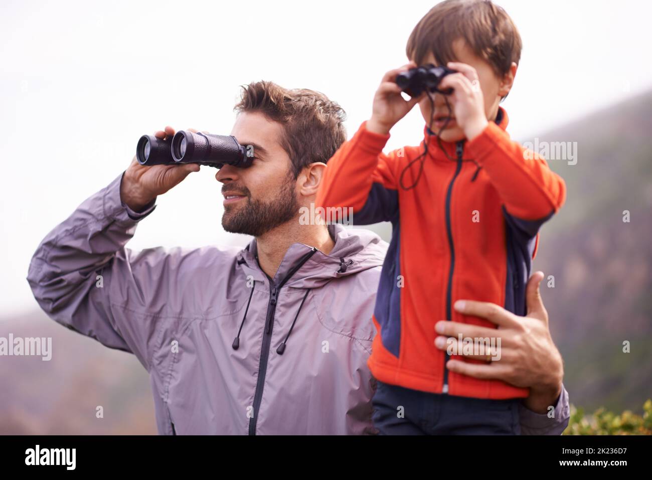 What do you see. a father and son looking through binoculars while on a ...