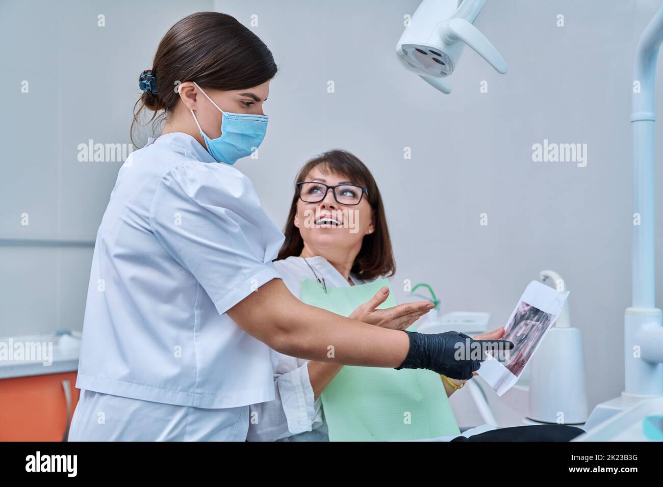 Female dentist talking to woman patient, discussing x-rays of teeth and ...