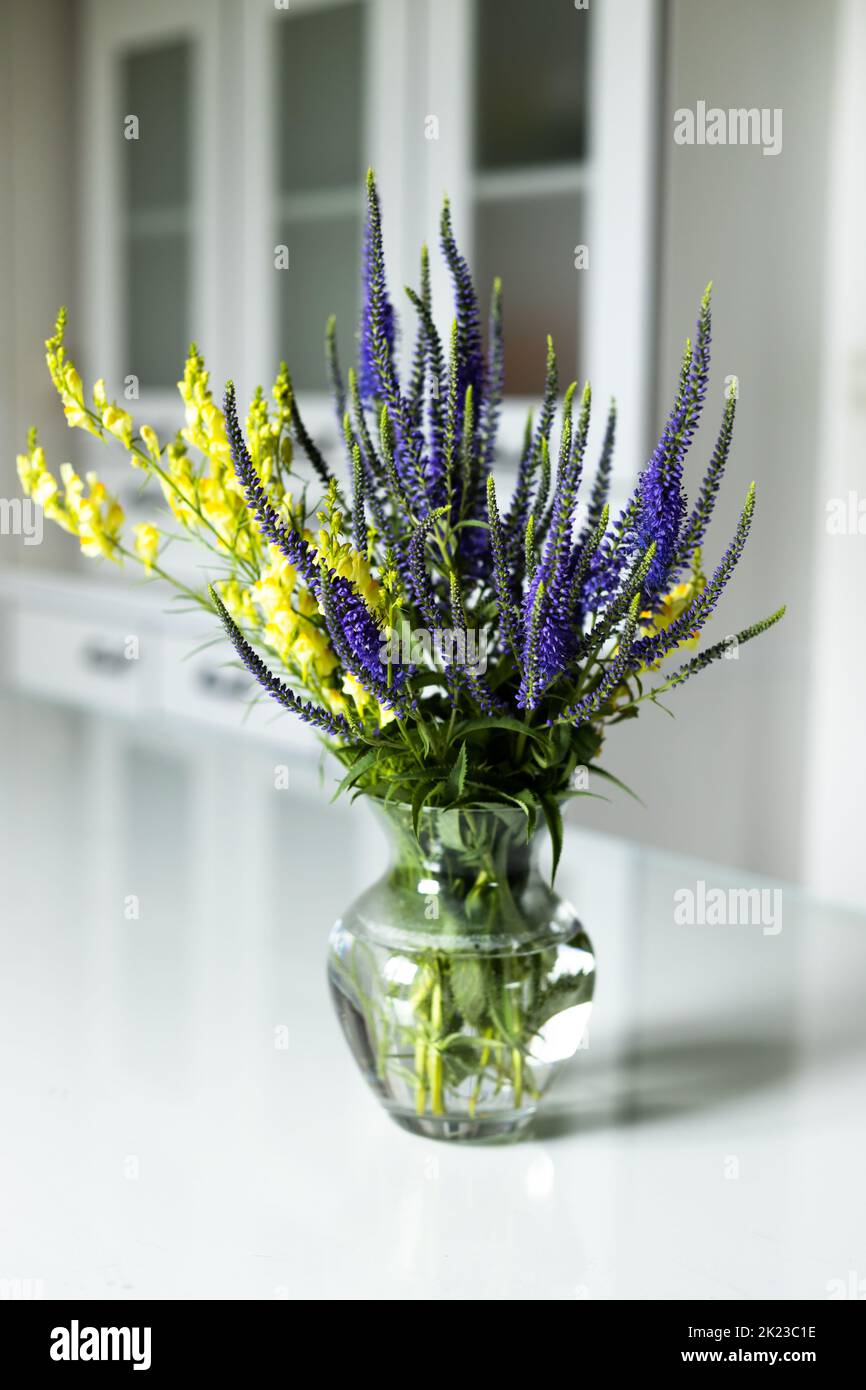 Bouquet of wild flowers in a glass vase on a white table. Purple ...