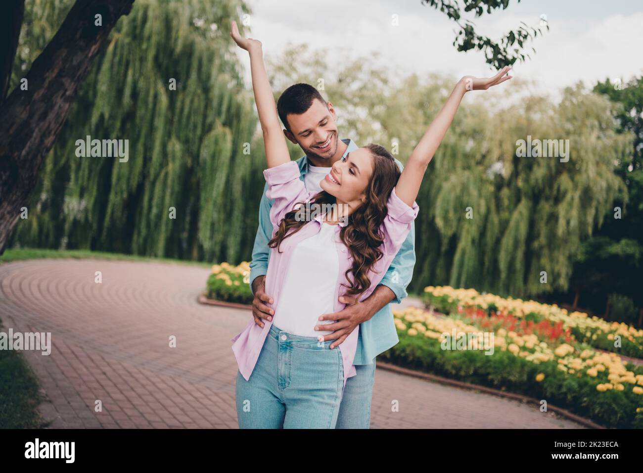Photo of two idyllic positive partners cuddle hug raise hands enjoy ...