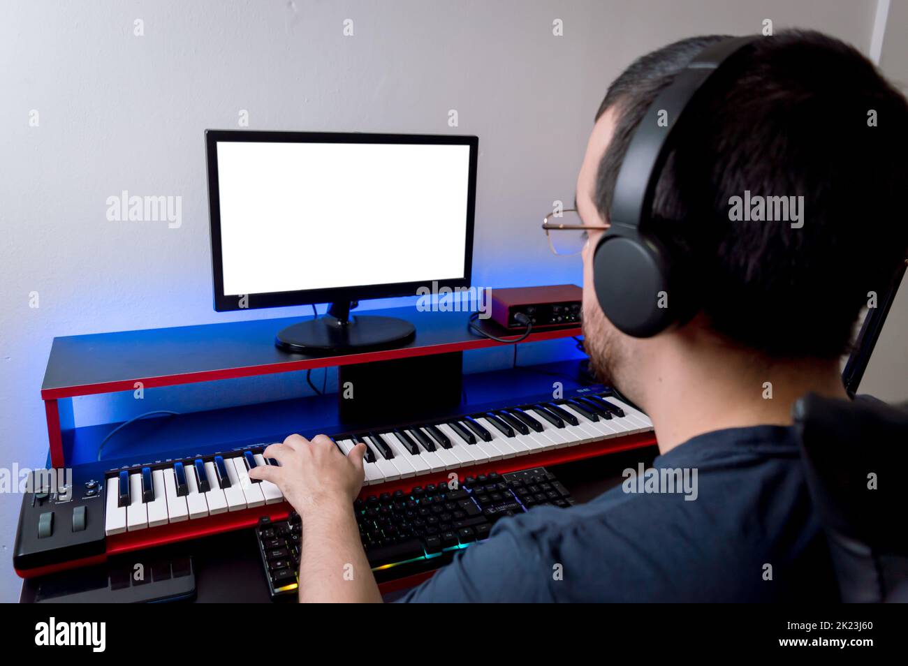 rear view of music producer with headphones, playing electric piano ...