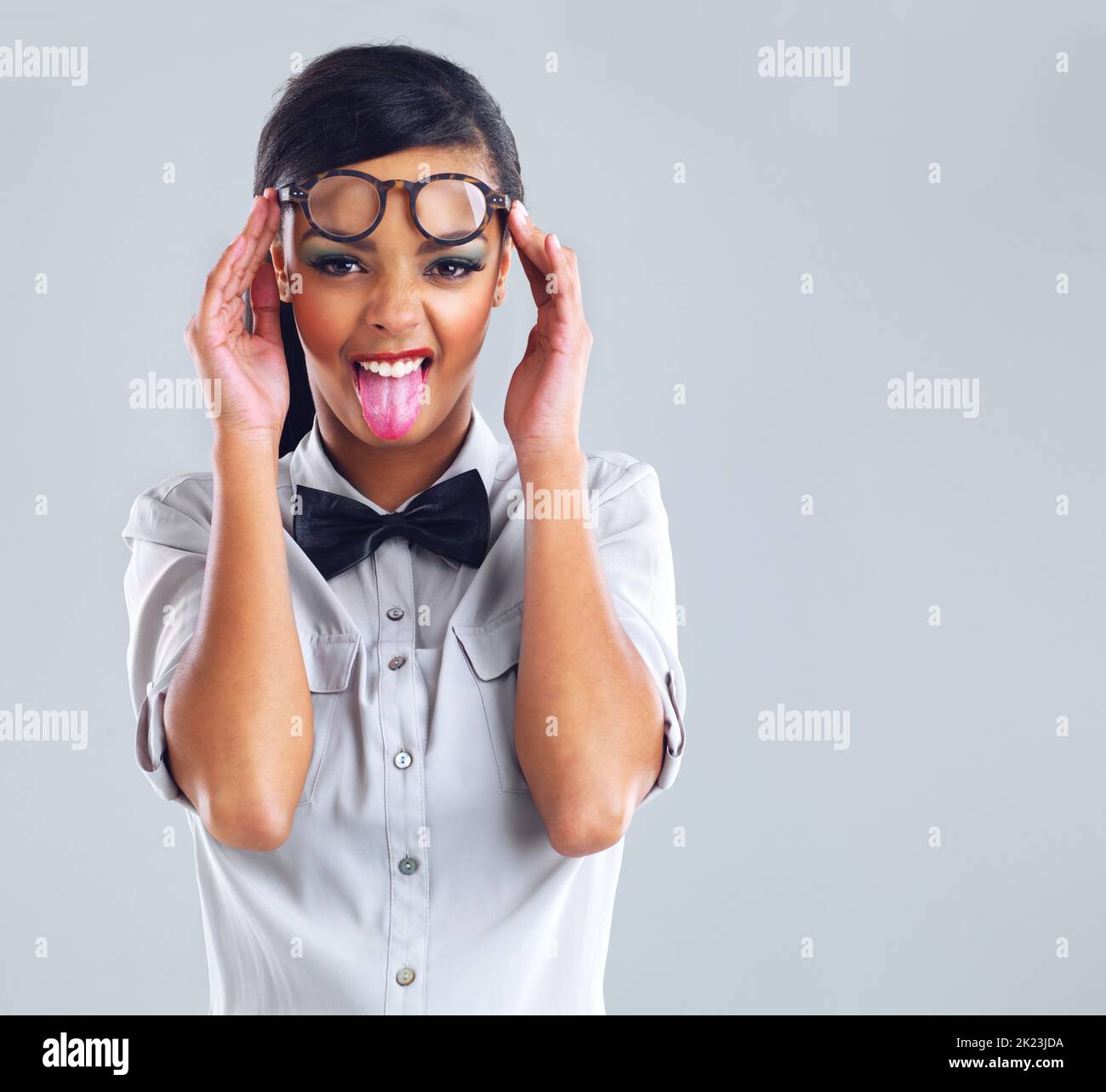 Making A Face Cropped Portrait Of A Trendy Young Woman Sticking Her Tongue Against A Gray