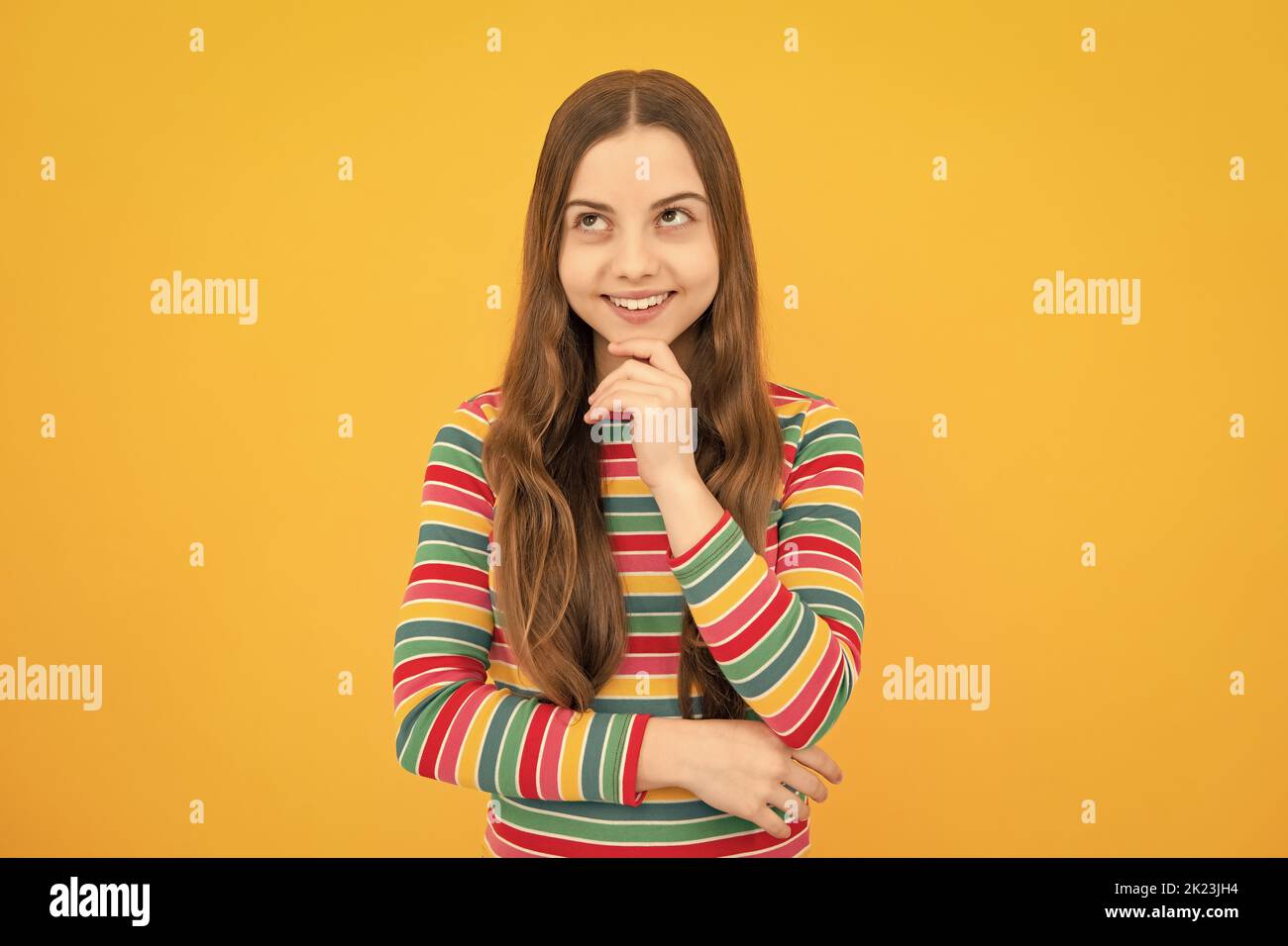 Smart nerdy school girl touching cheek and thinking against yellow ...
