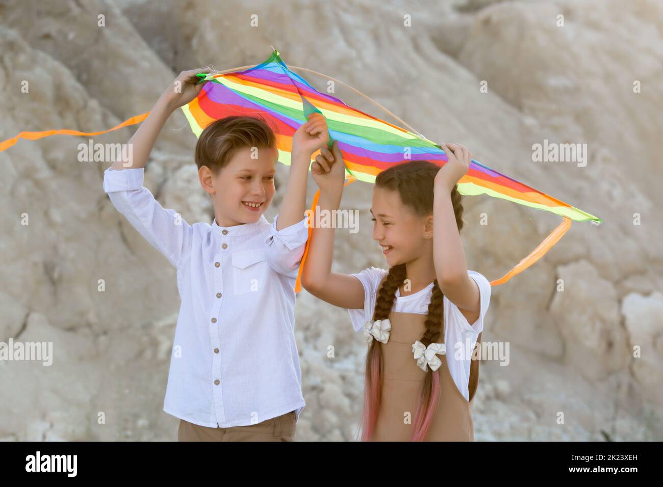 A girl and a boy carry a bright colored kite over their heads while ...