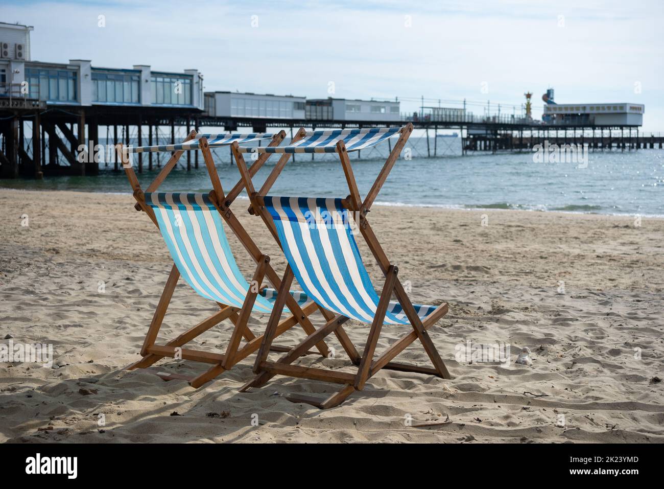 Pair of blue and white deck chairs on a sandy beach with Sandown pier ...