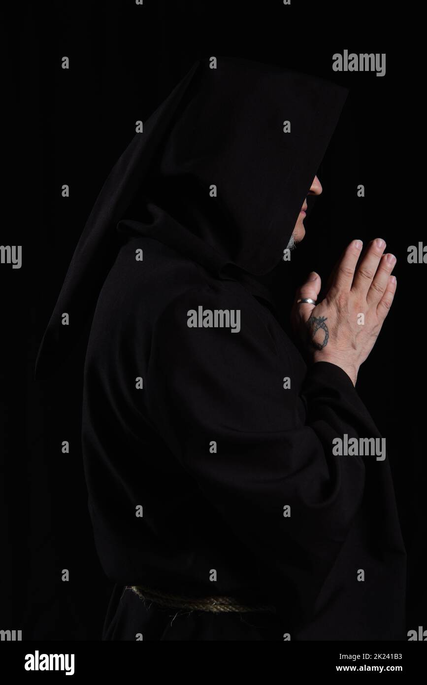 side view of tattooed priest with obscured face praying isolated on ...