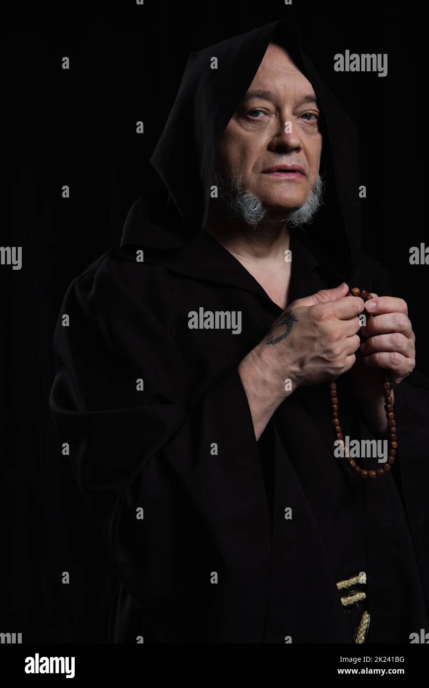 senior medieval monk with rosary looking at camera isolated on black ...