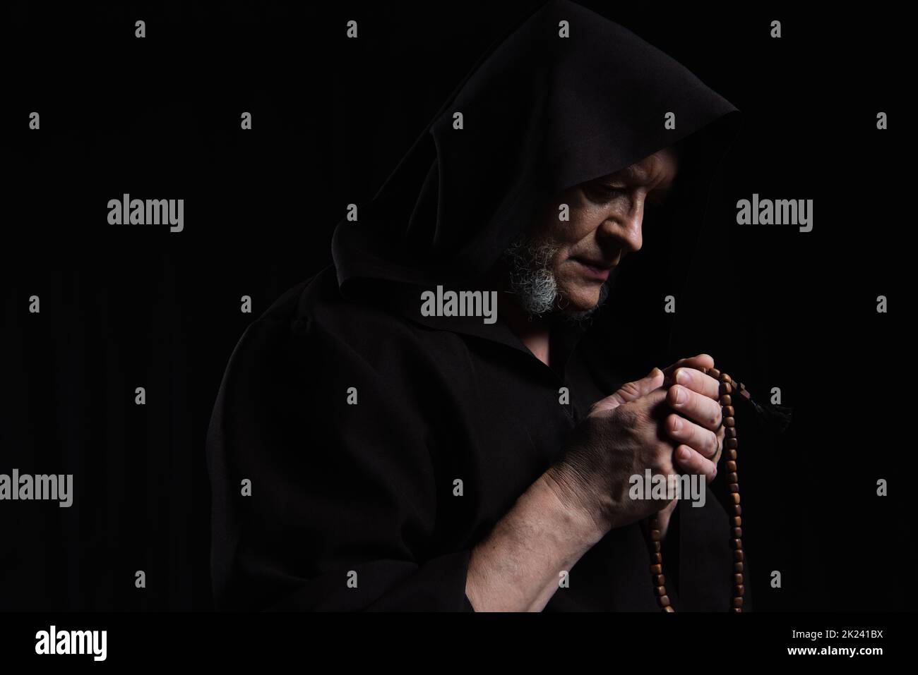 mysterious priest in hooded robe praying with rosary beads isolated on ...