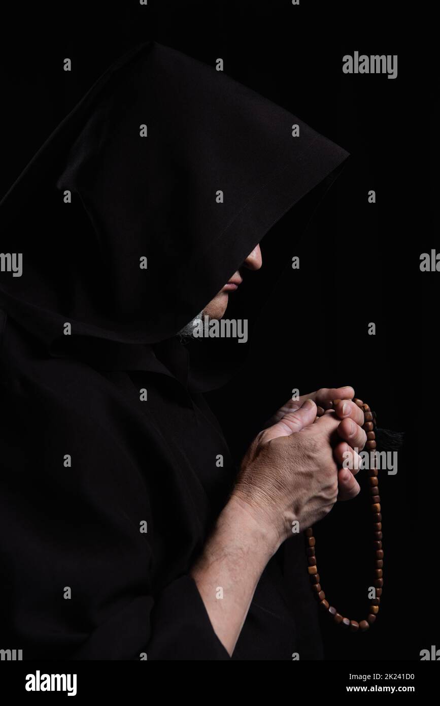 side view of mysterious monk with face obscured under hood praying with ...